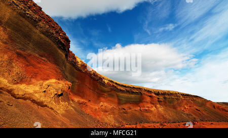 Colorful deposits of volcanic ash in reds and yellows against a green ...
