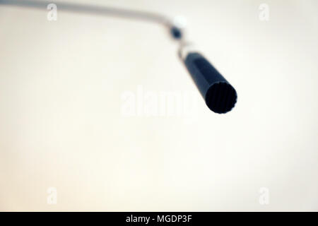 An isolated studio microphone hanging from above by it's cord facing ...