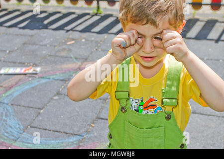 Cute boy cries. Kid cries on a playground. A child rubbed his eyes. A ...