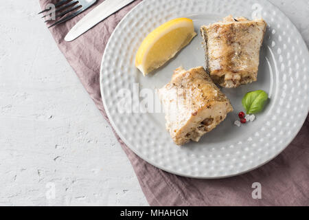 Baked Pollock fish with lemon and spices on a plate Napkin on the table ...