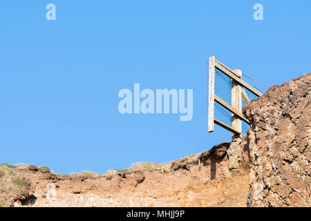 Ground eroded away by storms leaves a fence hanging over the edge of a ...