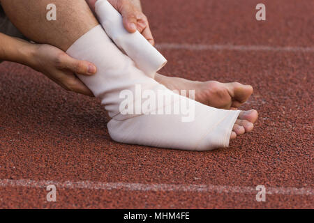 Male athlete applying compression bandage onto ankle injury of a ...