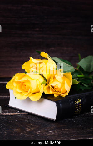Yellow roses laying on a Bible, wooden background. Free space for your ...