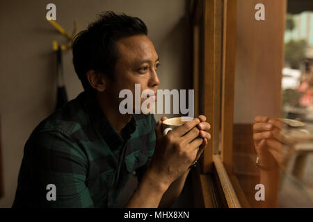 Thoughtful male entrepreneur with coffee cup seen through glass window ...