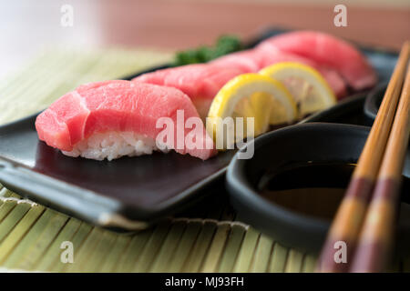 Otoro tuna sushi on black plate along with Japanese sauce and green ...
