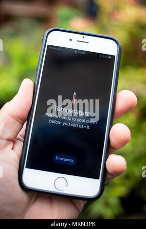A hand holding a smartphone displaying a temperature warning message ...