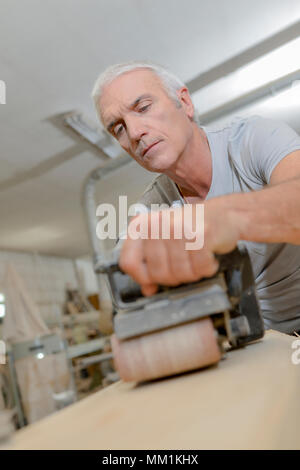 Senior carpenter sanding a wood with belt sander in carpentry workshop ...
