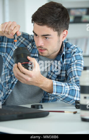A man fixing photo camera lens on an office table Stock Photo - Alamy