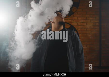 A cloud of vapor. Vaping man holding a mod. Brick background. Vape ...