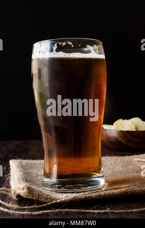 Full shaker pint glass of amber ale or beer on wooden table with grey ...