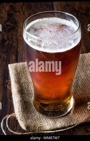 Full shaker pint glass of amber ale or beer on wooden table with grey ...