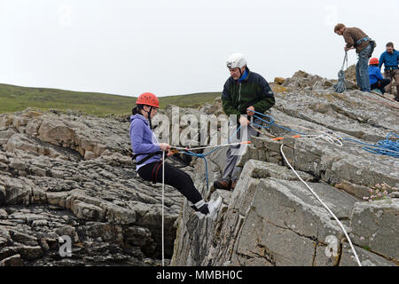 Climbers club climbing and abseiling on cliffs next to the sea. A ...