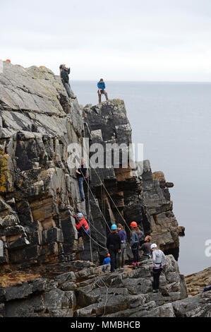 Climbers club climbing and abseiling on cliffs next to the sea. A ...