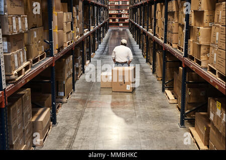 Single warehouse worker in between large racks of cardboard boxes on ...
