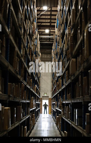 Single warehouse worker in between large racks of cardboard boxes on ...