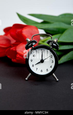 Black alarm clock near bouquet red tulips and red apple on black ...