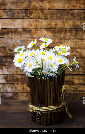 Beautiful chamomile flowers in wicker basket near white wall, closeup ...