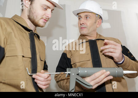 apprentice and workers using silicone pistol Stock Photo - Alamy