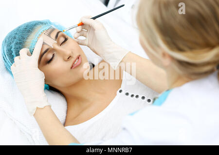 Professional beautician is going to correct eyebrow line at woman face ...