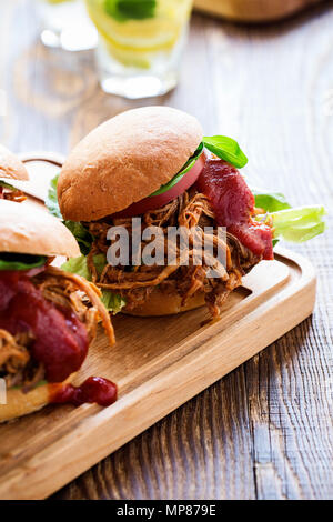 Pulled pork sandwiches with leaf vegetables, tomato on wooden board on ...