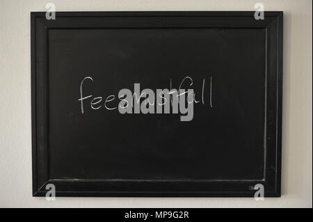 Fees Must Fall written in white chalk on a wall mounted blackboard ...