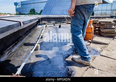 Heating and melting of bitumen surface by flame from gas torch. Worker ...