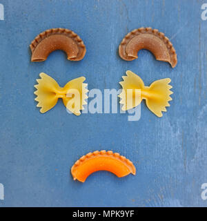 sad face with raw pasta on blue background Stock Photo - Alamy
