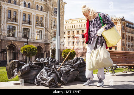 A homeless man looking through a garbage can bin in affluent area of ...