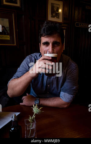 Brazilian man holding pint of dark beer and taking a sip in an ...