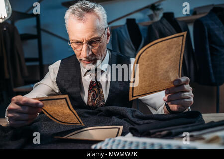 Mature tailor working with cut patterns at sewing workshop in late ...