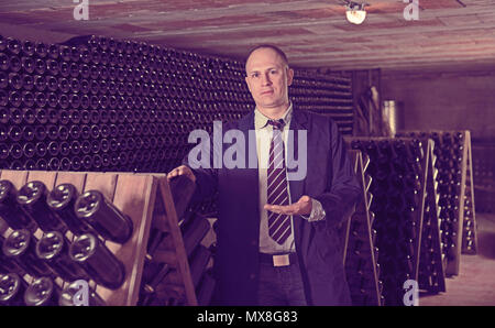 Male winemaker giving tour around winery, showing wine cellar with wine ...