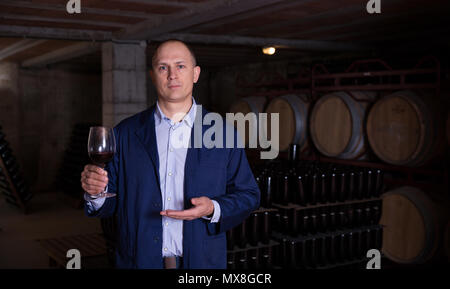 Male winemaker giving tour around winery, showing wine cellar with wine ...