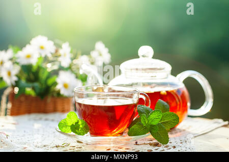Cup with hot tea with mint and a thyme on a wooden table in a summer ...