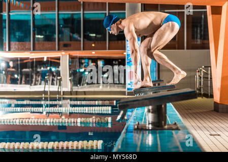 Man standing on diving board at public swimming pool above the water ...