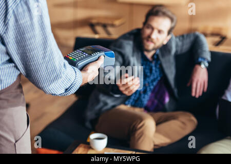 cropped shot of waiter holding payment terminal while smiling woman ...