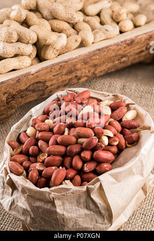 Paper bag full of peeled peanuts and peanuts in nutshell on a piece of ...