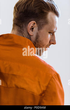 Male prisoner in orange uniform sits on the bed, reads Bible in prison ...