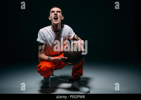 Screaming man in prison uniform and cuffs holding rosary and praying on ...