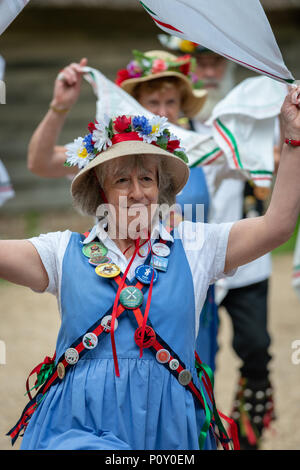 A morris dancer wearing a hat covered in summer flowers and wearing a ...