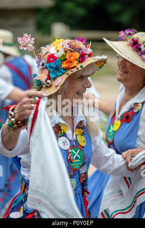 A morris dancer wearing a hat covered in summer flowers and wearing a ...