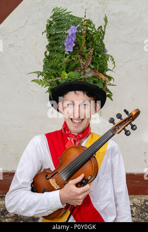 A morris dancer wearing a hat covered in summer flowers and wearing a ...