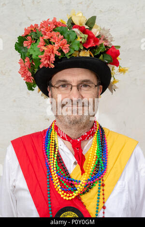 A morris dancer wearing a hat covered in summer flowers and wearing a ...