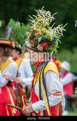 A morris dancer wearing a hat covered in summer flowers and wearing a ...