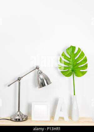 Vase with tropical leaves, picture and lamp on table near dark brick ...