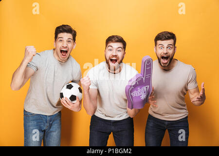 Three young cheery men football fans celebrating isolated over yellow ...