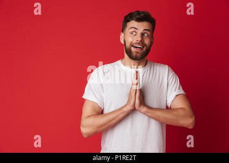 Picture of hopeful young man standing isolated over red wall background ...