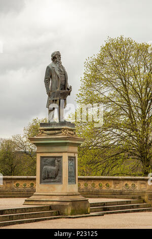 Statue on plinth in paved walled garden with metal bench between small ...