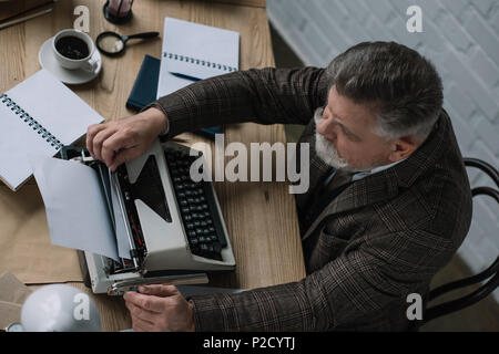 high angle view of senior writer working with laptop and making notes ...