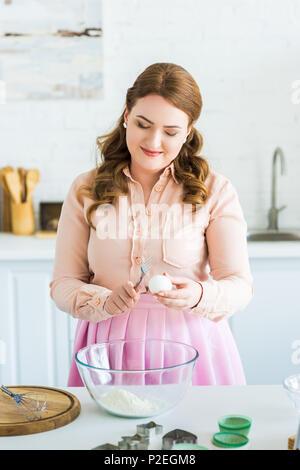 Woman breaking egg into bowl with flour at table against black ...