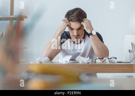 depressed student studying at table with crumpled papers and eyeglasses ...